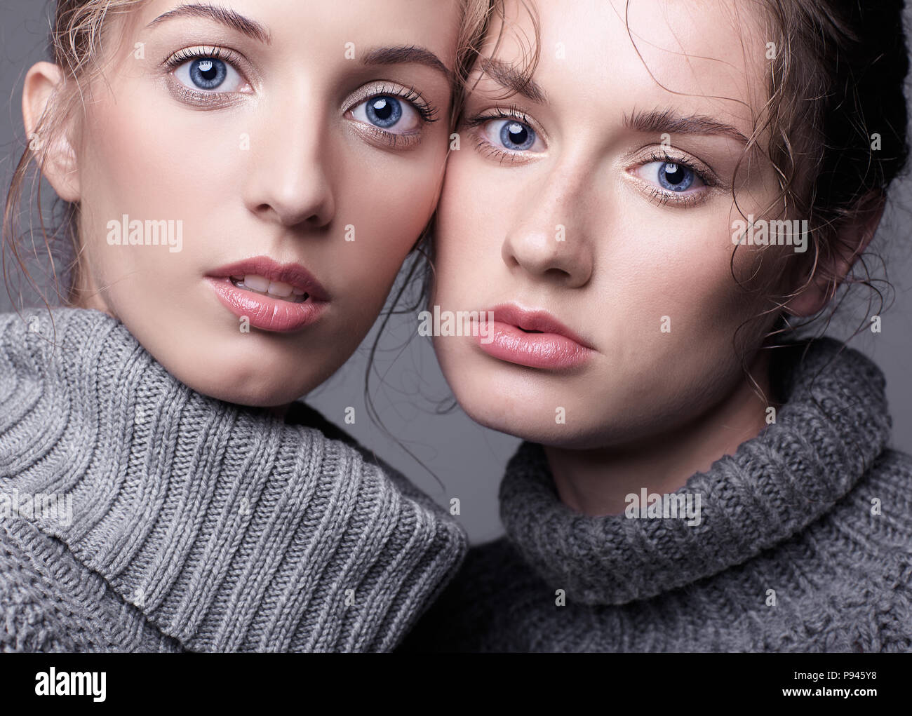 Two young women in gray sweaters on grey studio background. Beautiful ...