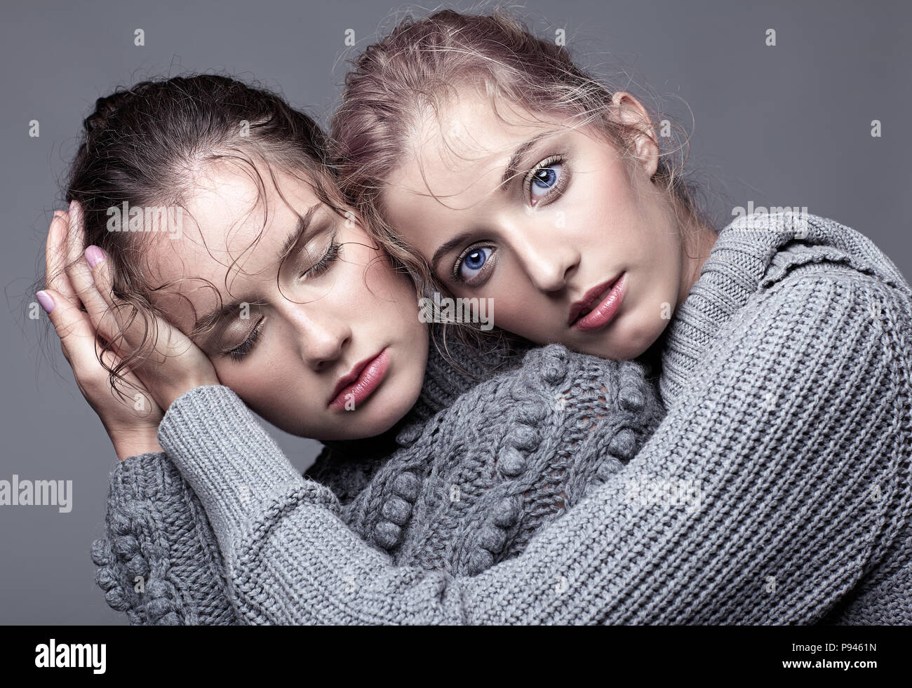Two young women in gray sweaters on grey studio background. Beautiful ...