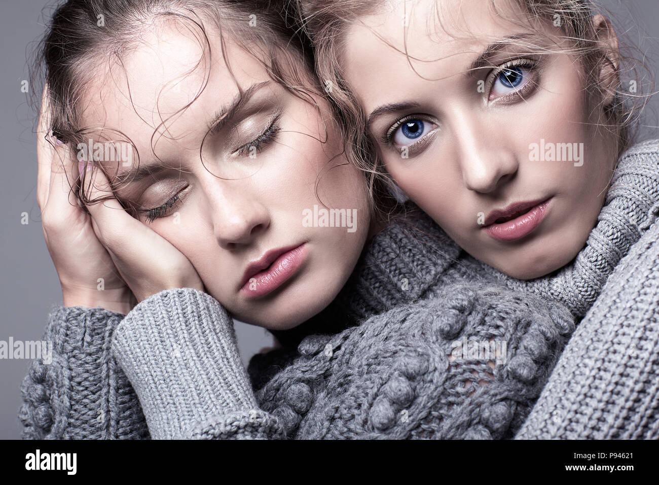 Two young women in gray sweaters on grey studio background. Beautiful ...