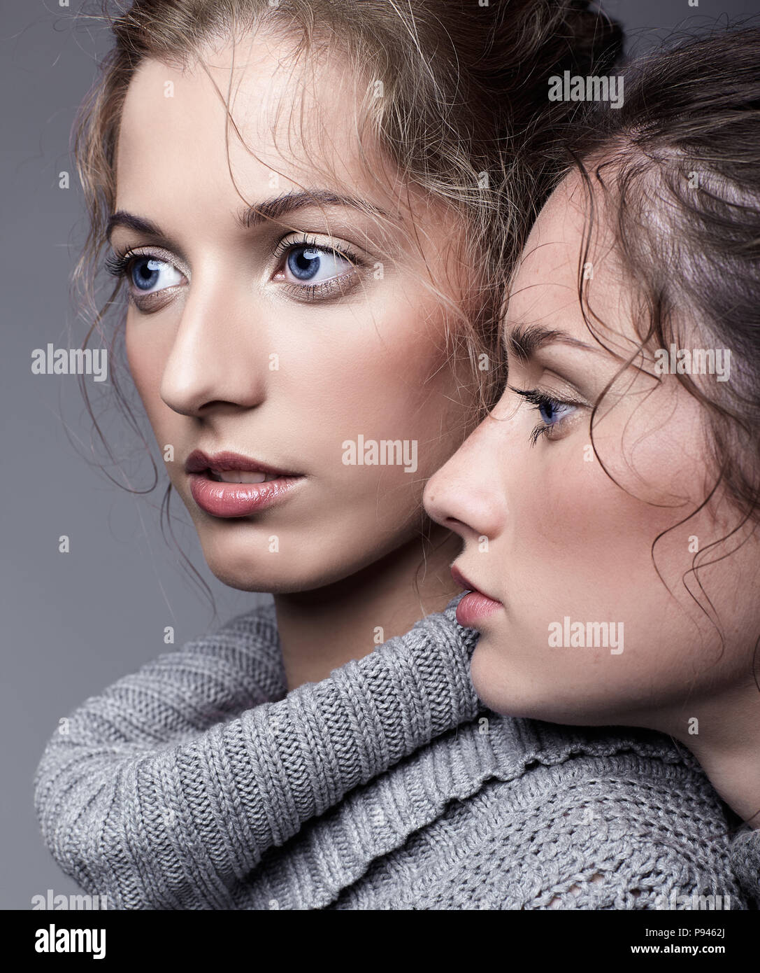 Two young women in gray sweaters on grey studio background. Beautiful ...