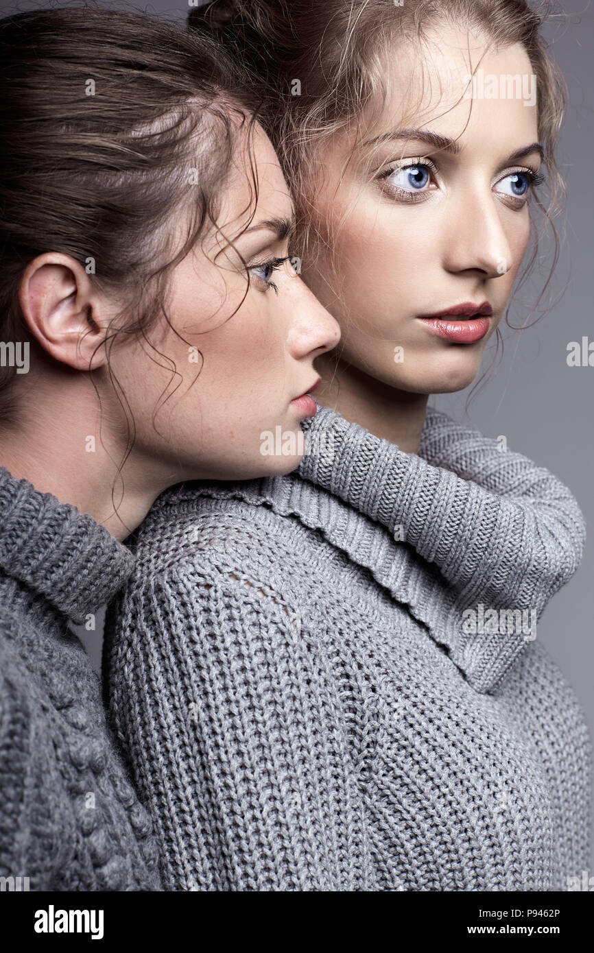Two young women in gray sweaters on grey studio background. Beautiful ...