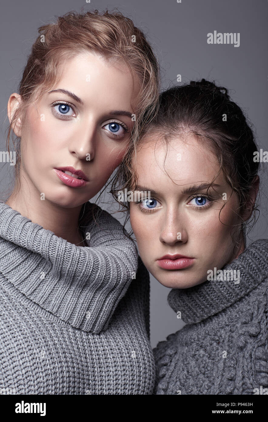 Two young women in gray sweaters on grey studio background. Beautiful ...
