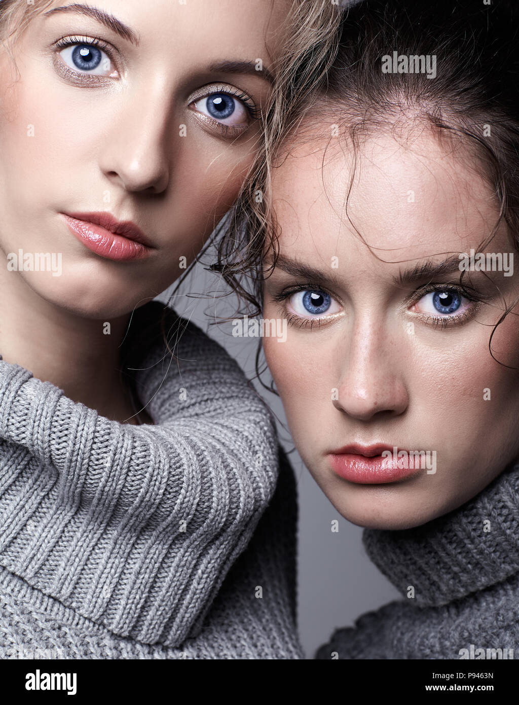 Two young women in gray sweaters on grey studio background. Beautiful ...