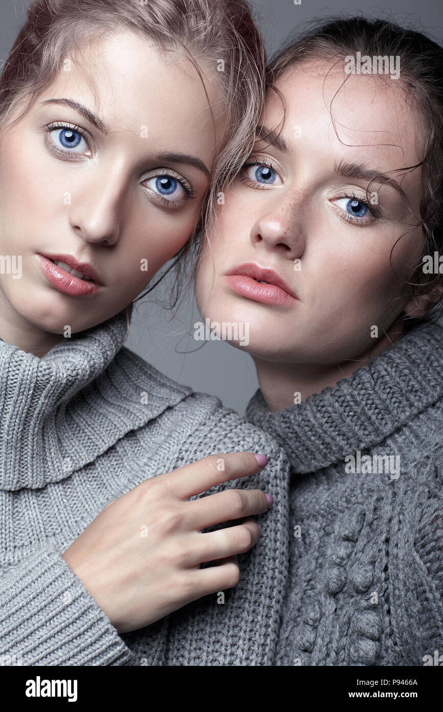 Two young women in gray sweaters on grey studio background. Beautiful ...