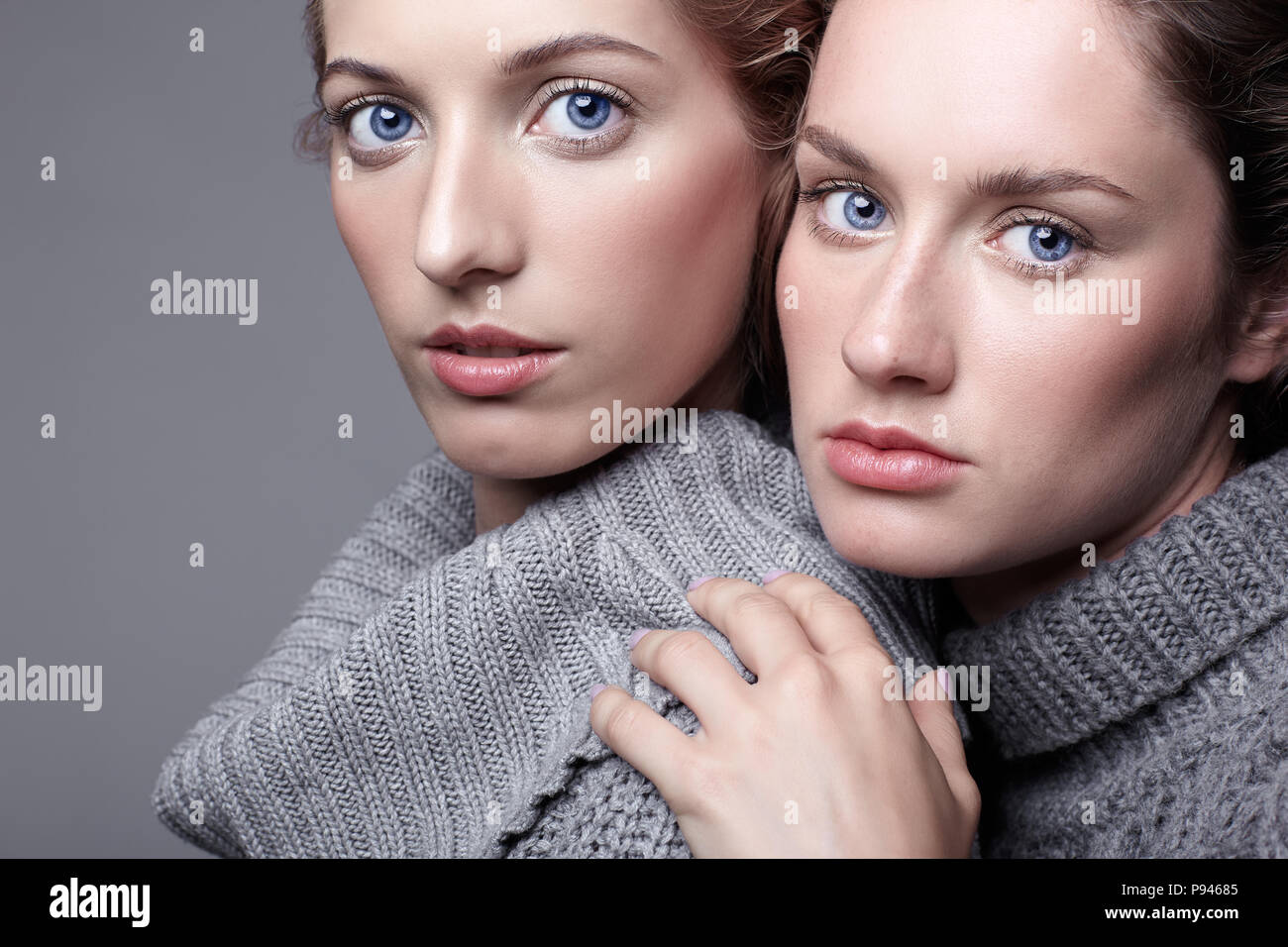 Two young women in gray sweaters on grey studio background. Beautiful ...