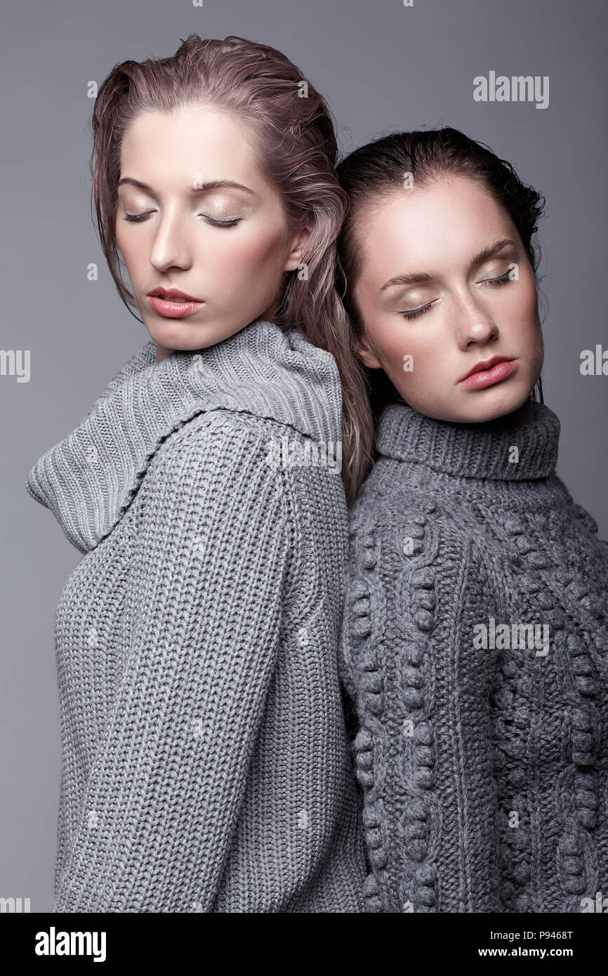 Two young women in gray sweaters on grey studio background. Beautiful ...