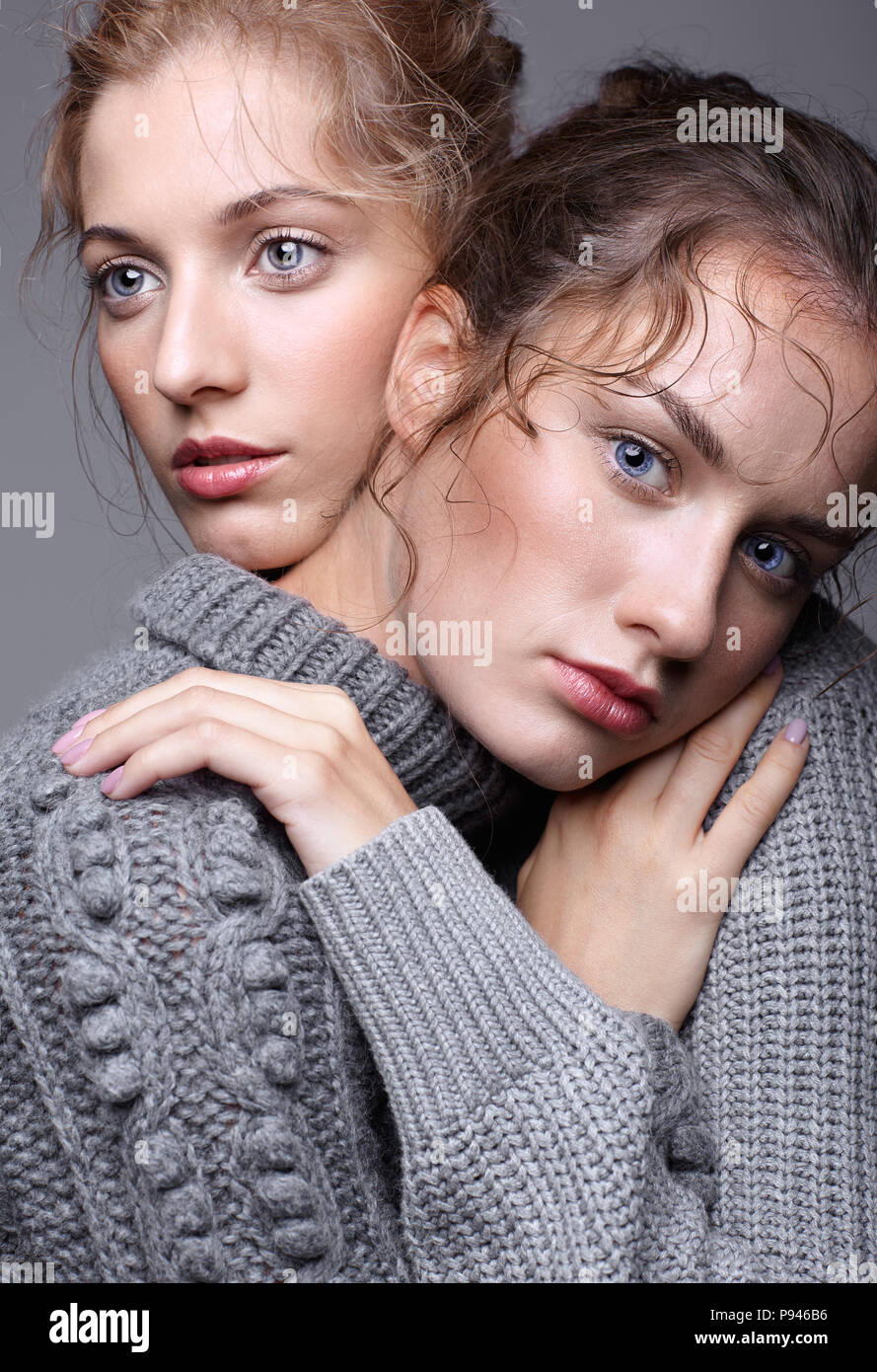 Two young women in gray sweaters on grey studio background. Beautiful ...