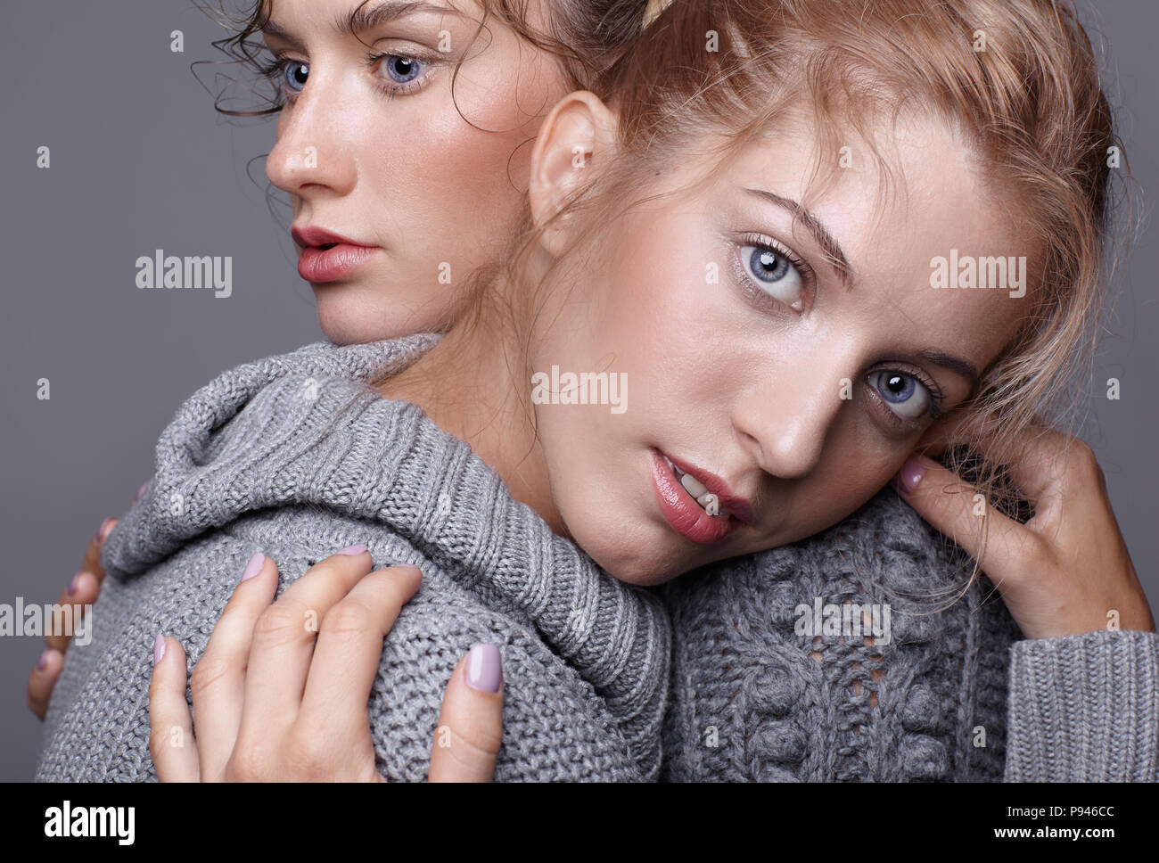 Two young women in gray sweaters on grey studio background. Beautiful ...