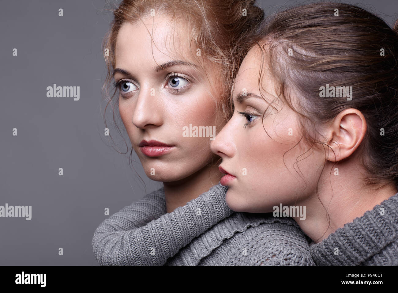 Two young women in gray sweaters on grey studio background. Beautiful ...