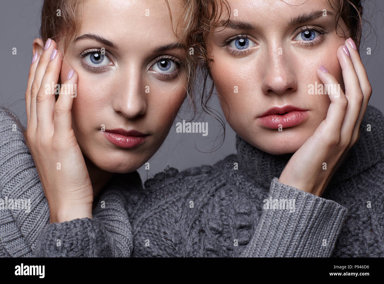 Two young women in gray sweaters on grey studio background. Beautiful ...
