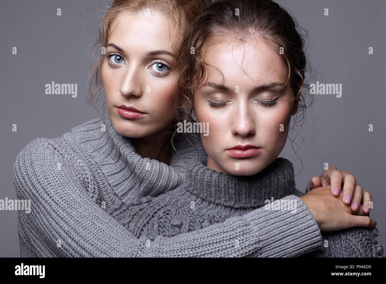 Two young women in gray sweaters on grey studio background. Beautiful ...