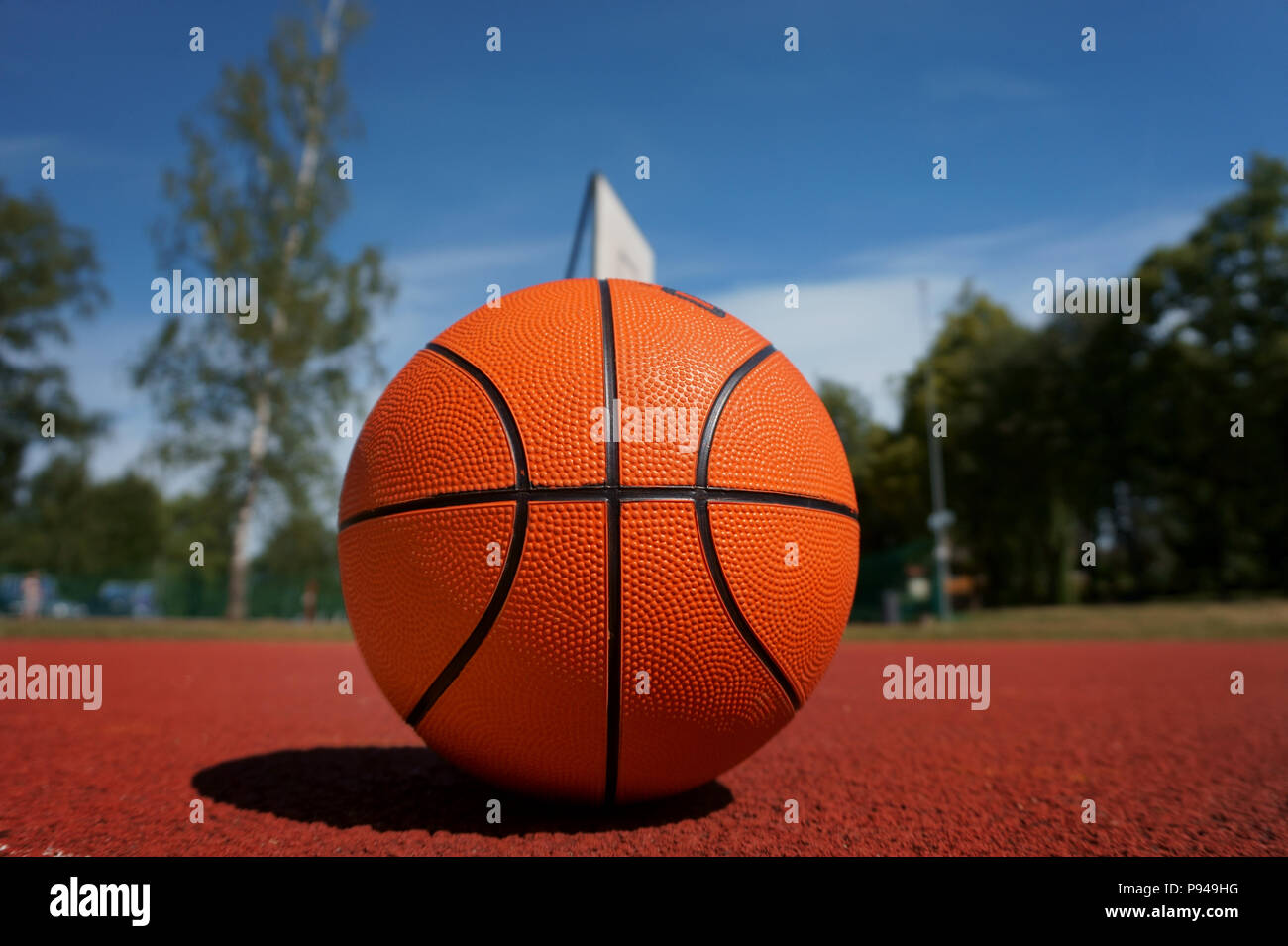 Basketball On Outdoor Basketball Court Floor Against The Trees And Blue basketball-on-outdoor-basketball-court-floor-against-the-trees-and-blue