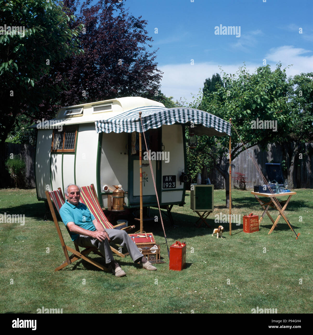 Portrait of man relaxing in old deckchair beside fifties caravan with ...