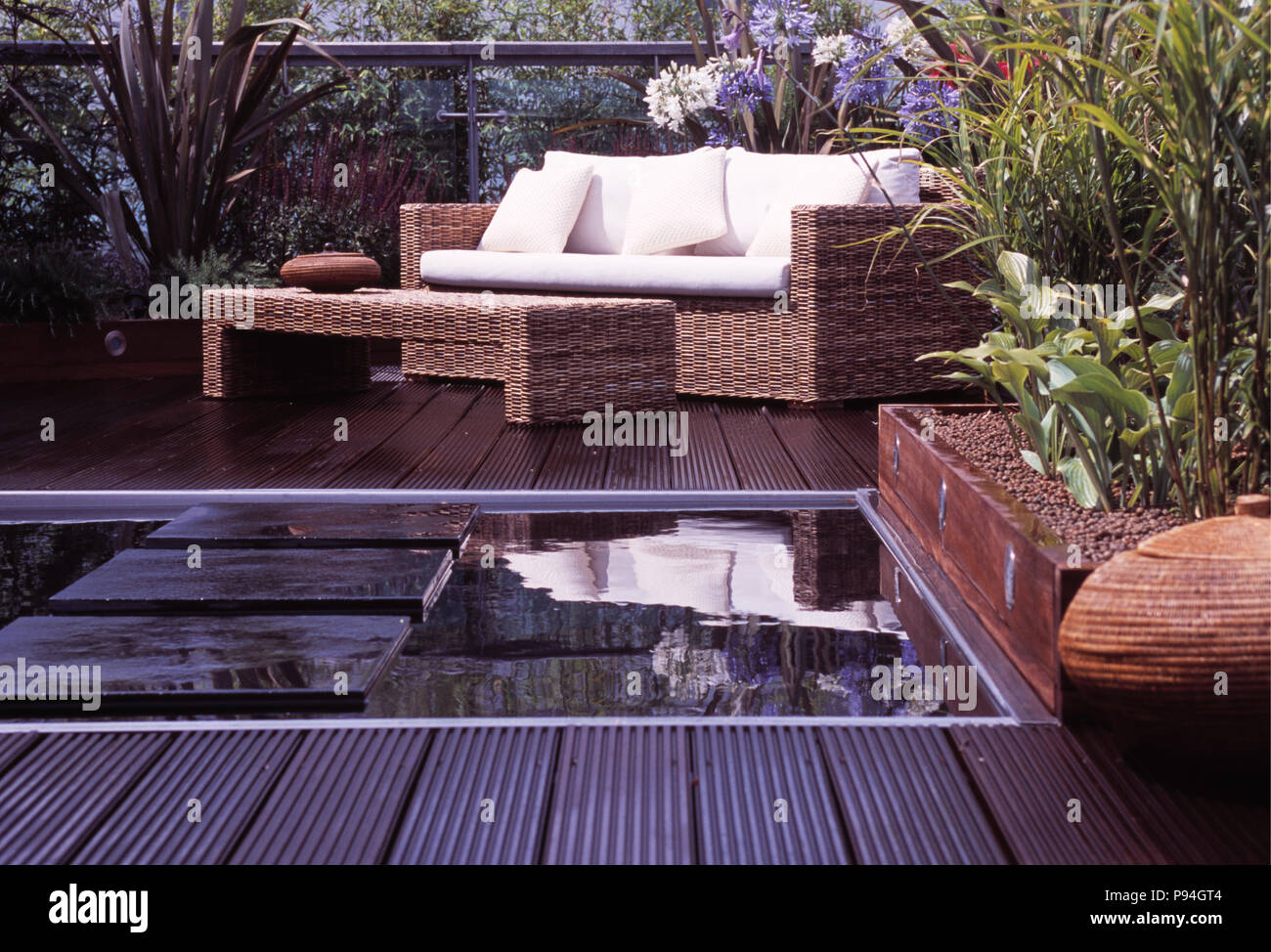 Shallow pool and raised beds in decked city roof terrace with wicker ...