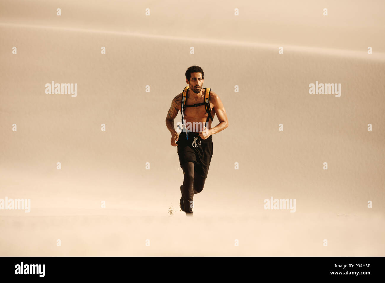 Full length of young muscular man running on sand dunes. Fit male ...