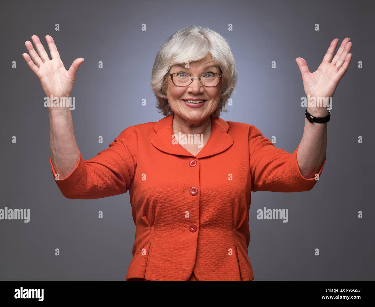 Happy senior lady with hands up on gray background with copy space ...