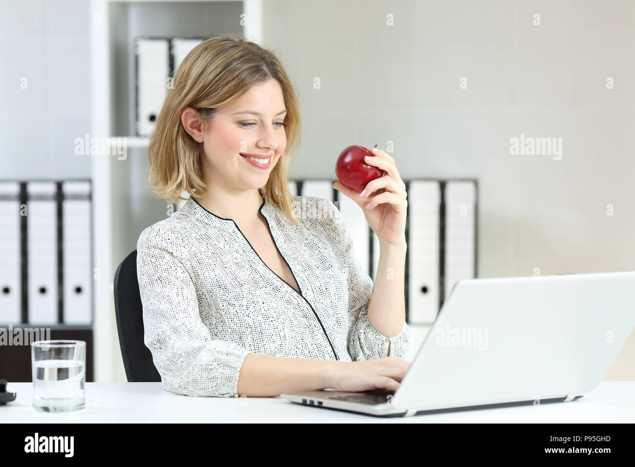 Happy office worker working online with a laptop holding an apple Stock ...