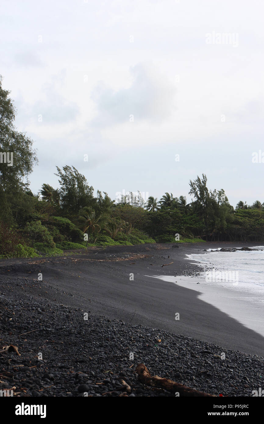 The black sand beach of Hana Bay, lined by a rainforest, in Hana, Maui ...