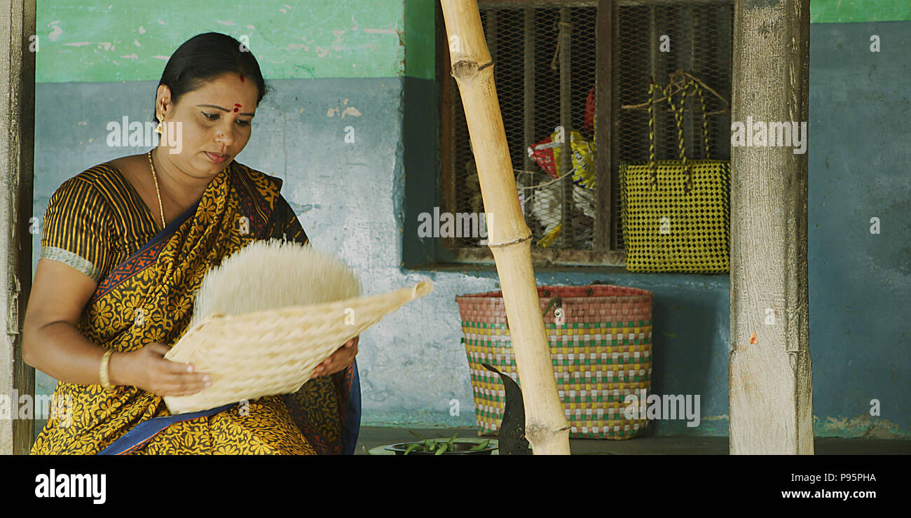 india woman sifting and cleaning rice outside her home in a rural ...
