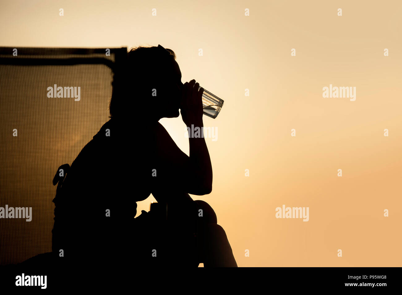 A woman drinks a glass of water, rehydrating in the hot summer sun ...