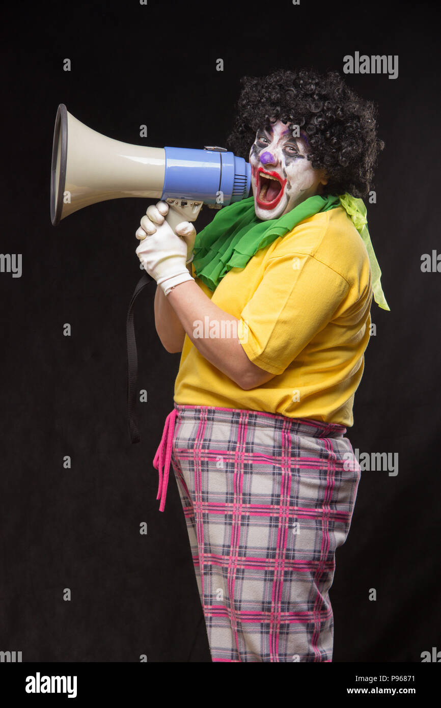 Scary evil clown shouting into a megaphone on a black background Stock ...