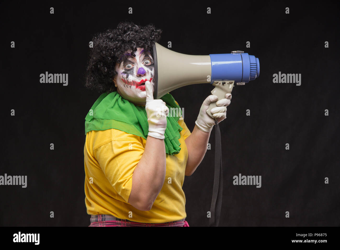 Scary evil clown shouting into a megaphone on a black background Stock ...