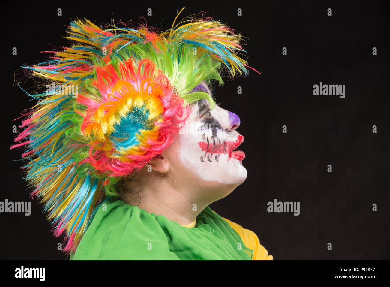 Scary clown with colorful mohawk and a smile with a lollipop on a black ...