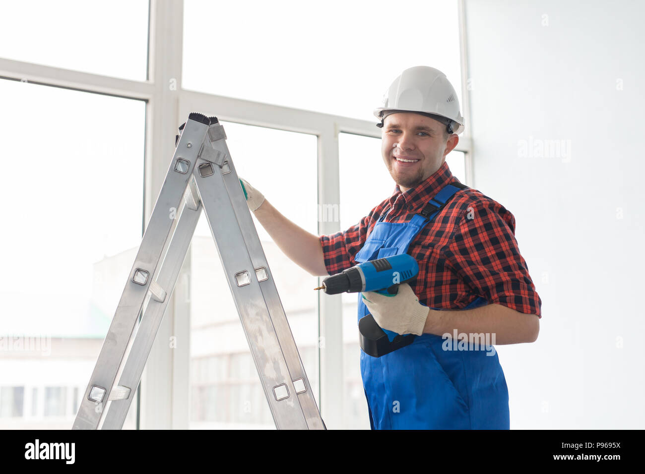 Happy male builder standing on ladder with drill infront of window ...