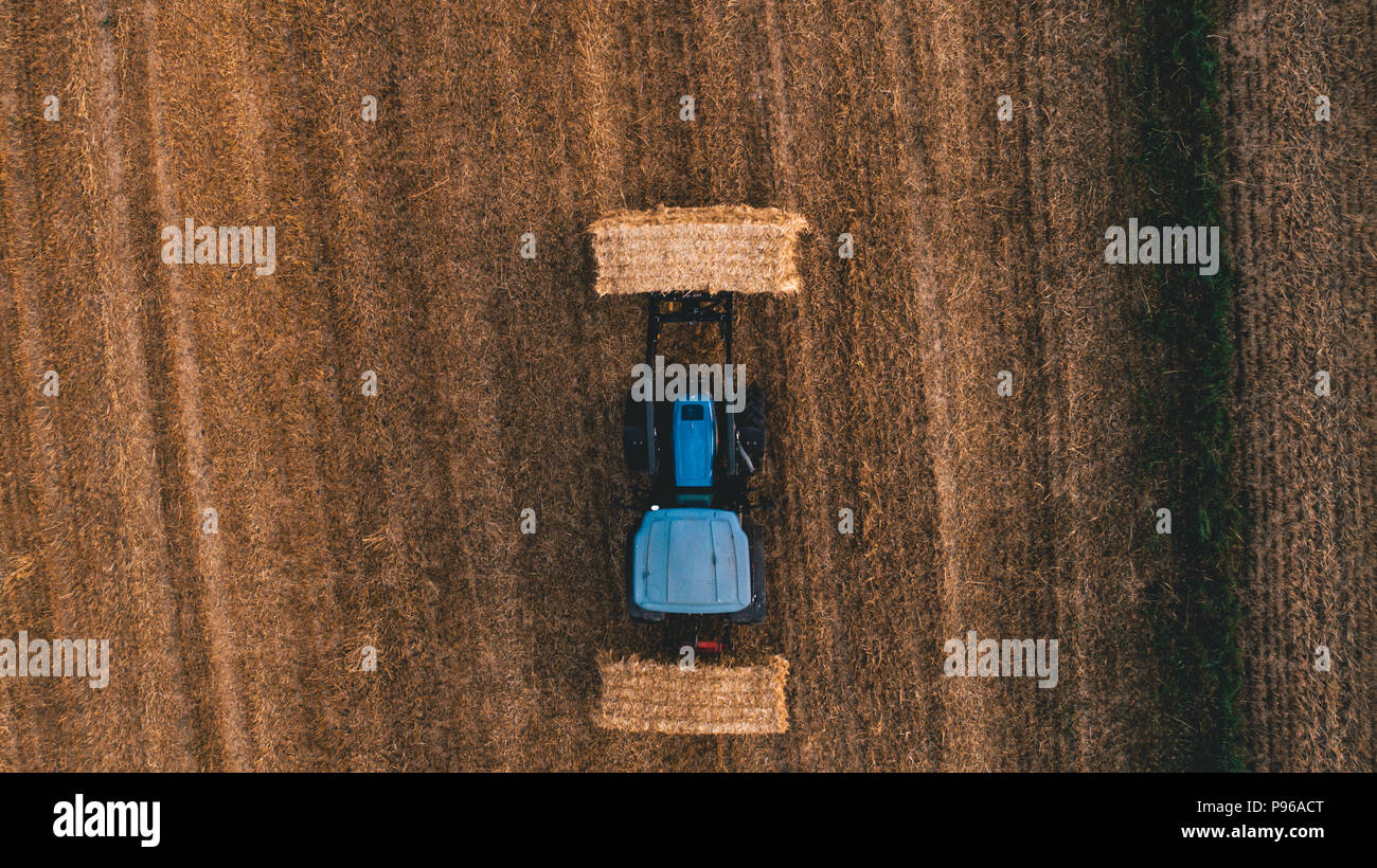 aerial view of harvest field with tractor moving hay bale around top ...