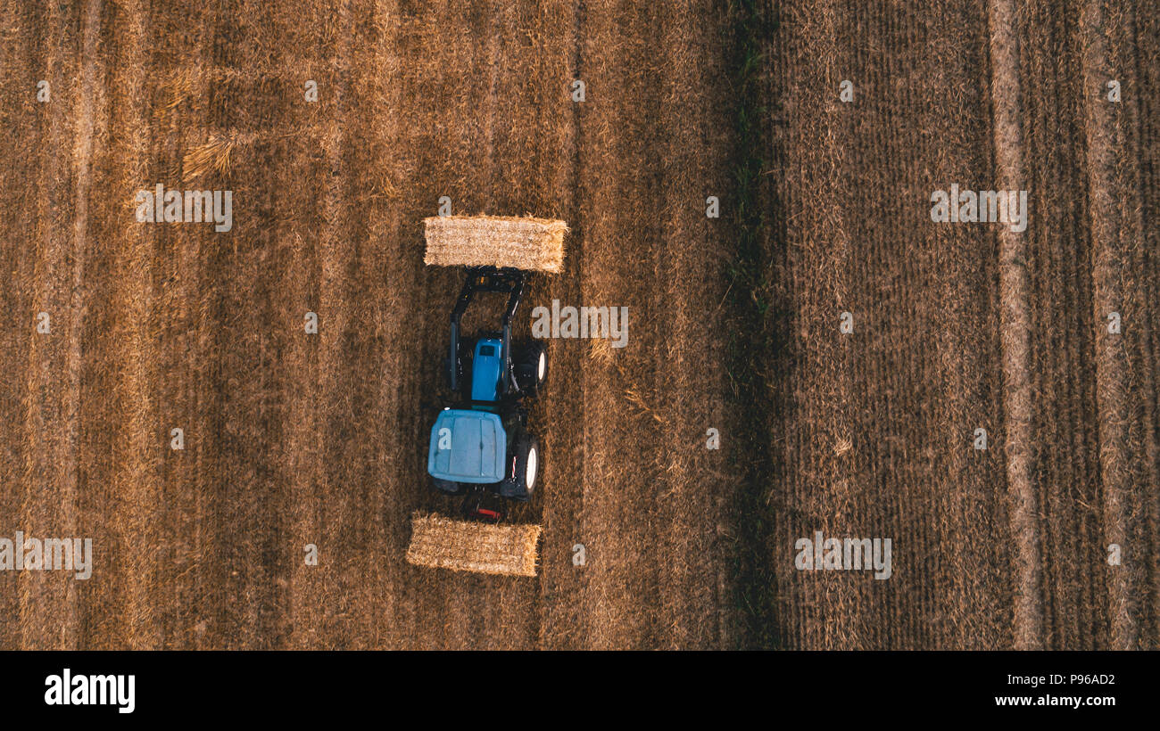 aerial view of harvest field with tractor moving hay bale around top ...
