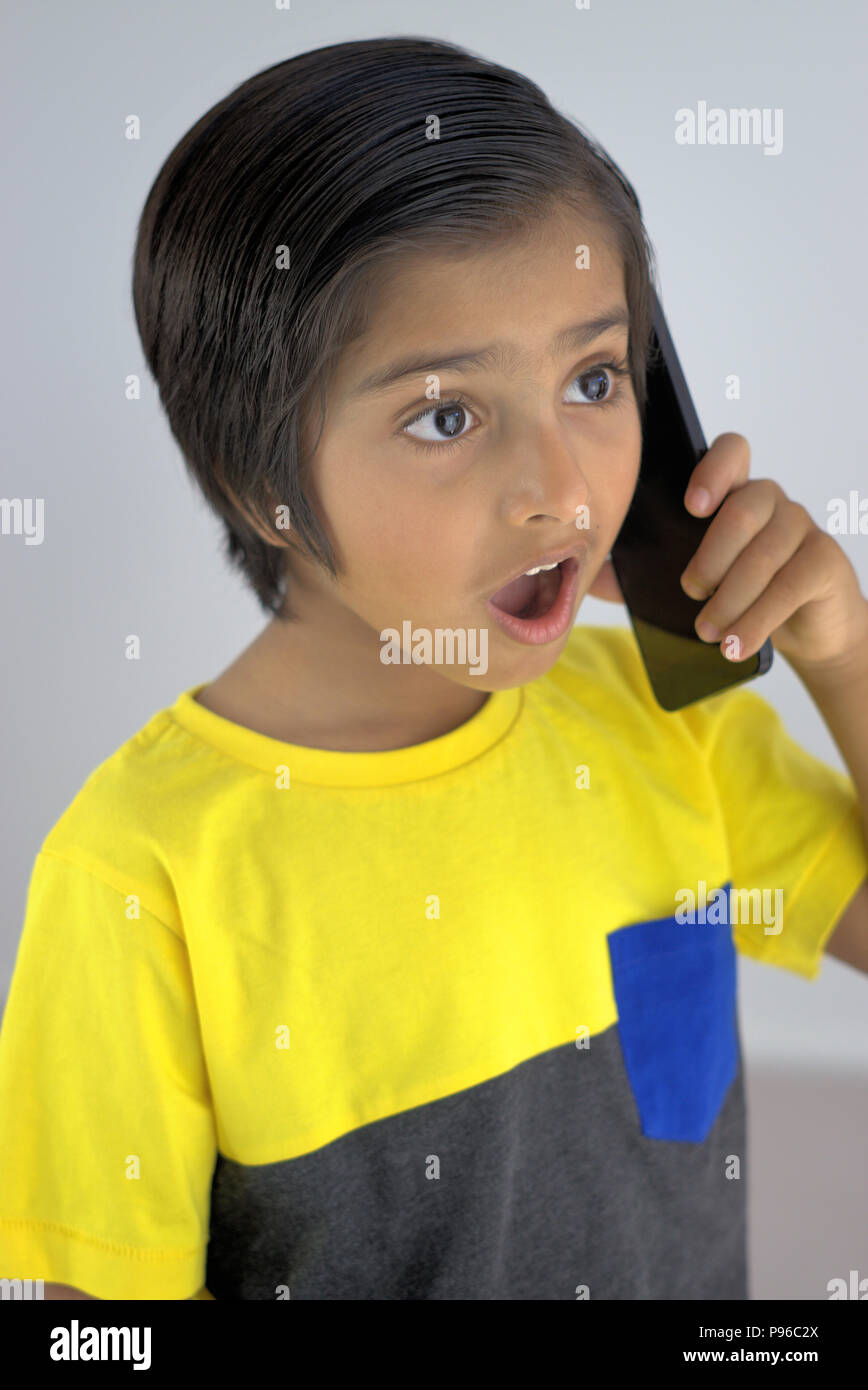 Happy kid talking on mobile phone. Surprised kid holding cell phone ...