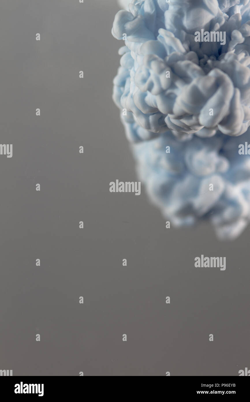 Light blue ink dropping into water and spreading on a light grey ...