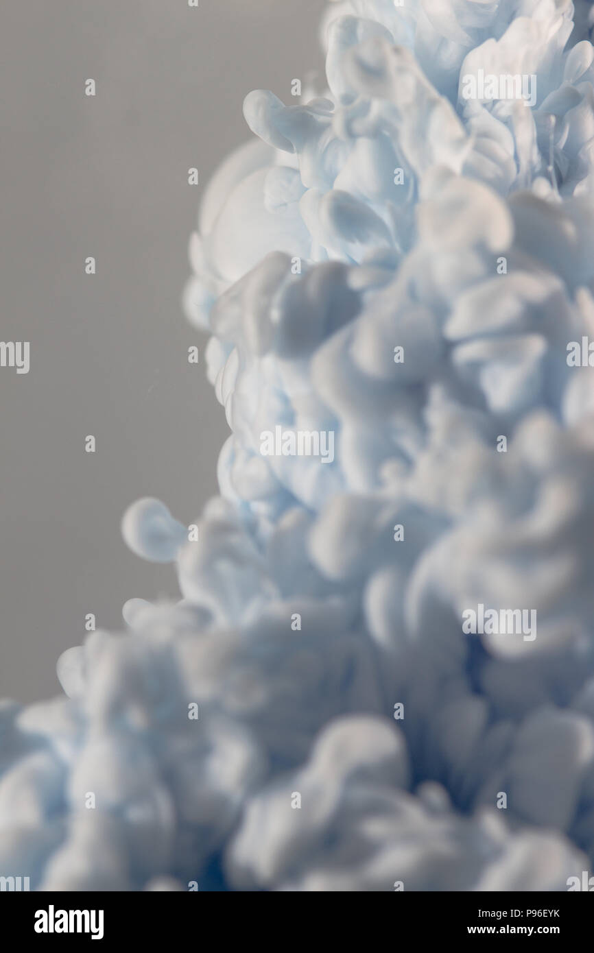 Light blue ink dropping into water and spreading on a light grey ...