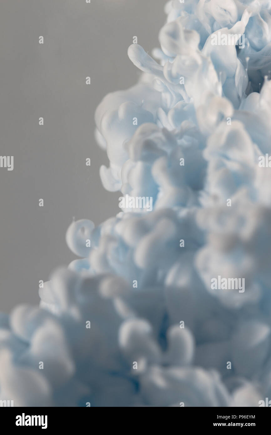 Light blue ink dropping into water and spreading on a light grey ...