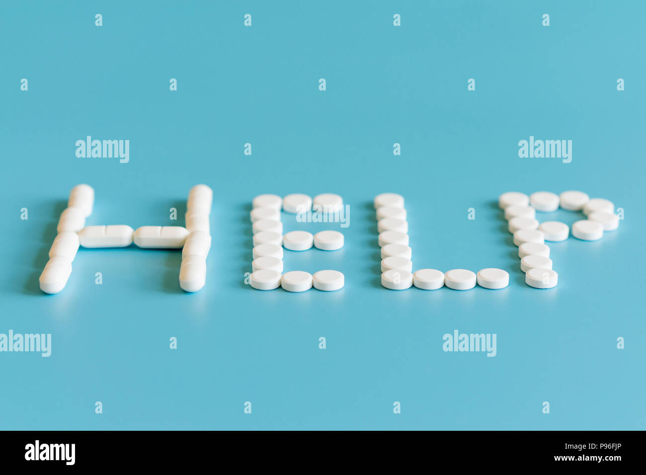 White pills on blue background word help. White medical pills on a blue ...