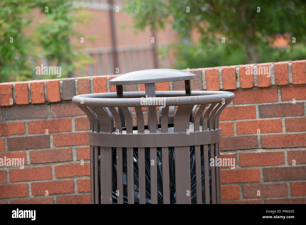 Large, round public garbage can against a red brick wall Stock Photo ...