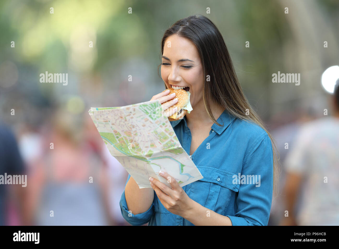 Happy tourist eating a burger and reading a paper map on vacation in ...