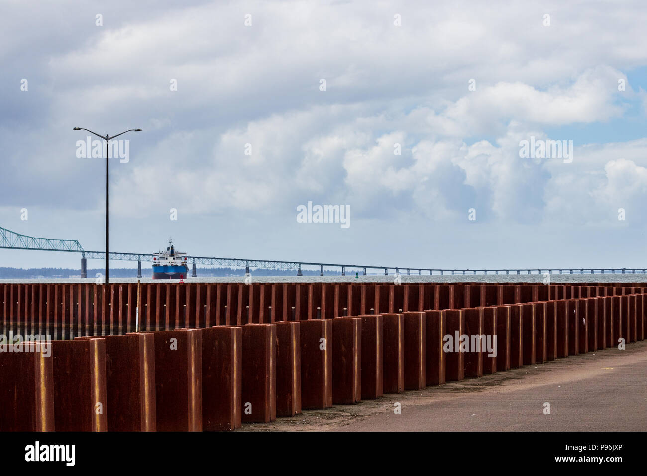 Cargo ship seen over a jetty near a bridge with heavy clouds and a lamp ...