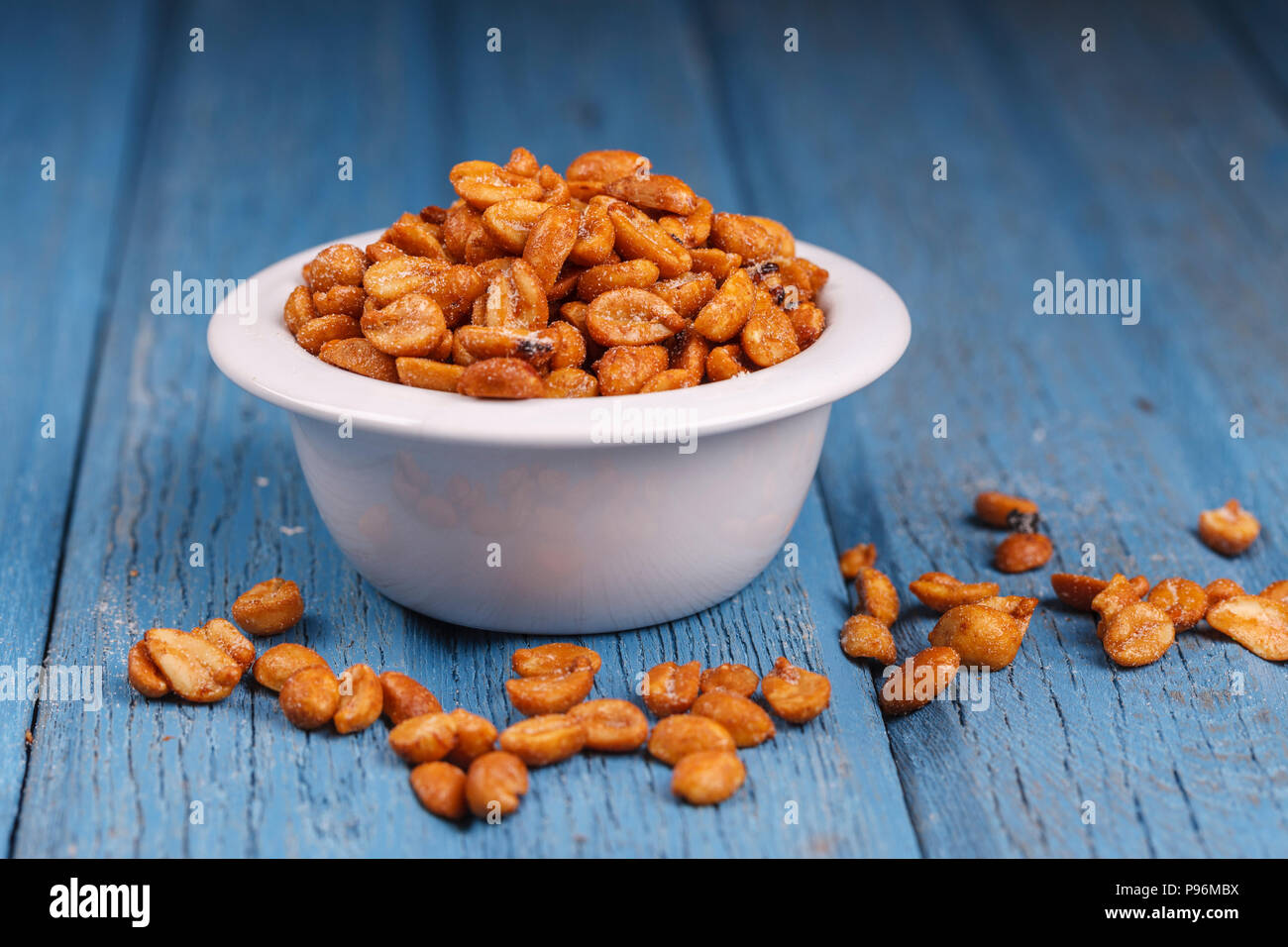 A studio image of roasted peanuts in a dish with some spilling over ...