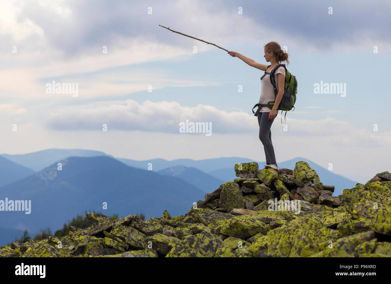 Young slim blond tourist girl with backpack points with stick at foggy ...