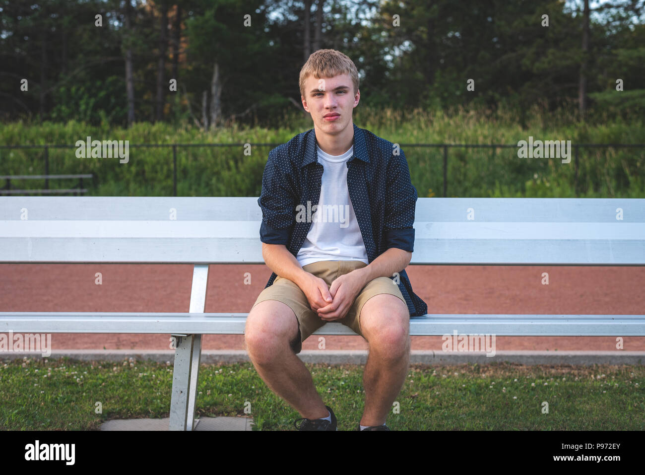 Sad teenager sitting on a school sports field team bench next to a ...