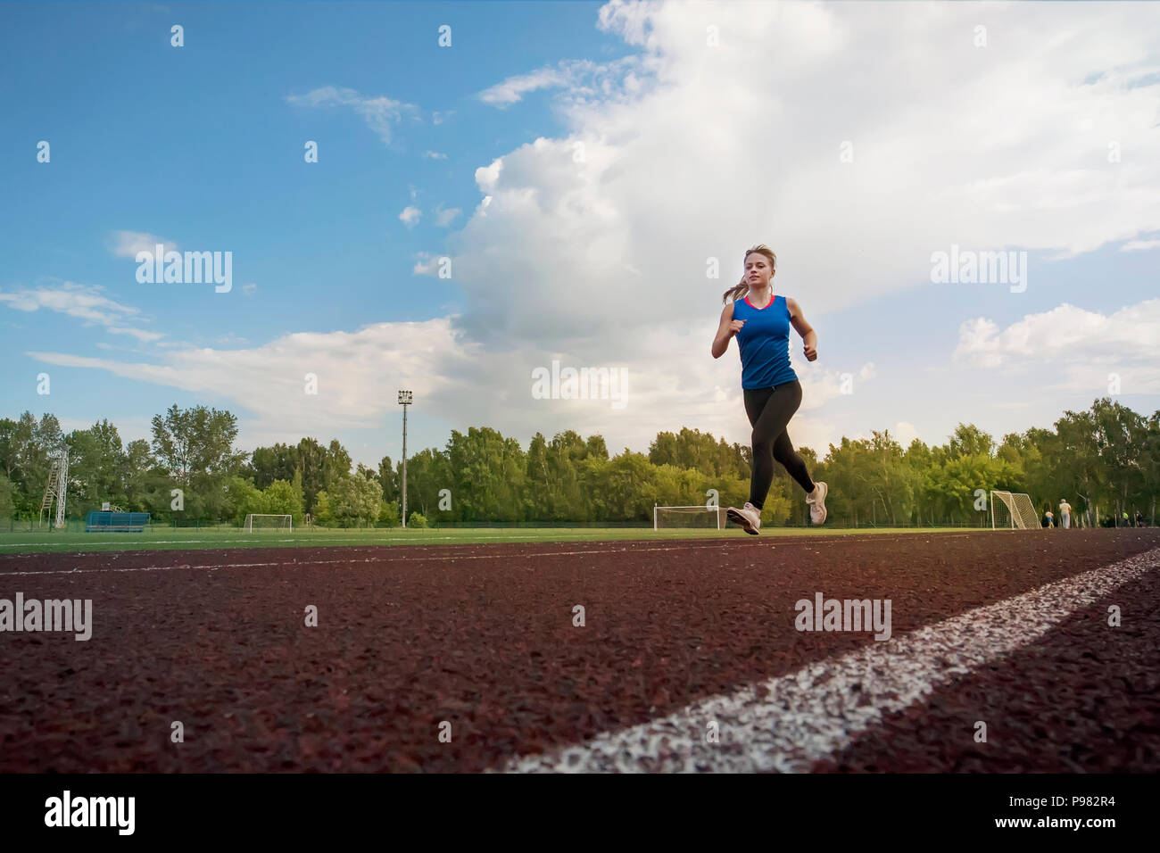 Athletic young blonde sportswoman sprinting on running track stadium ...