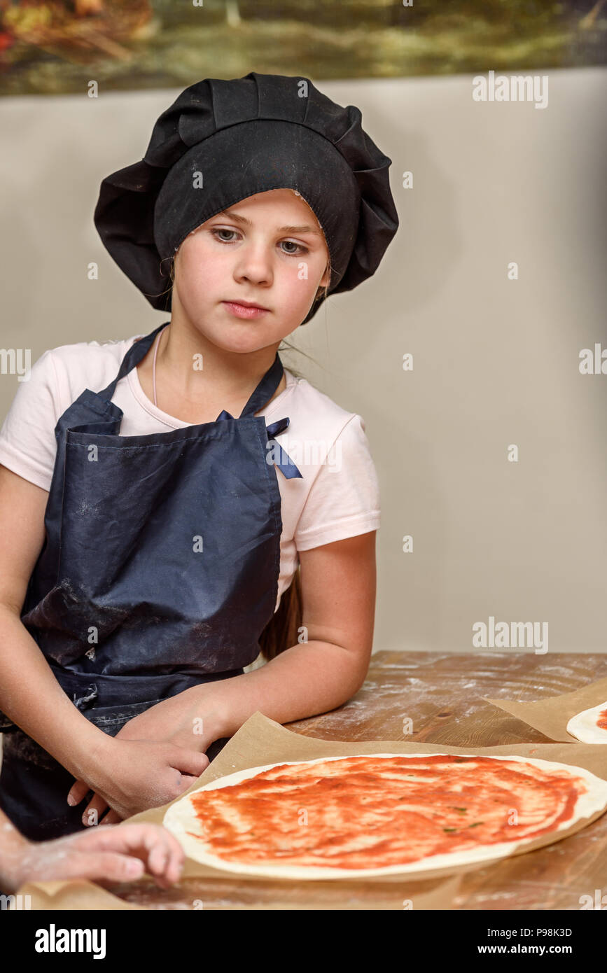 Little girl cook in uniform prepares pizza in the kitchen Stock Photo ...