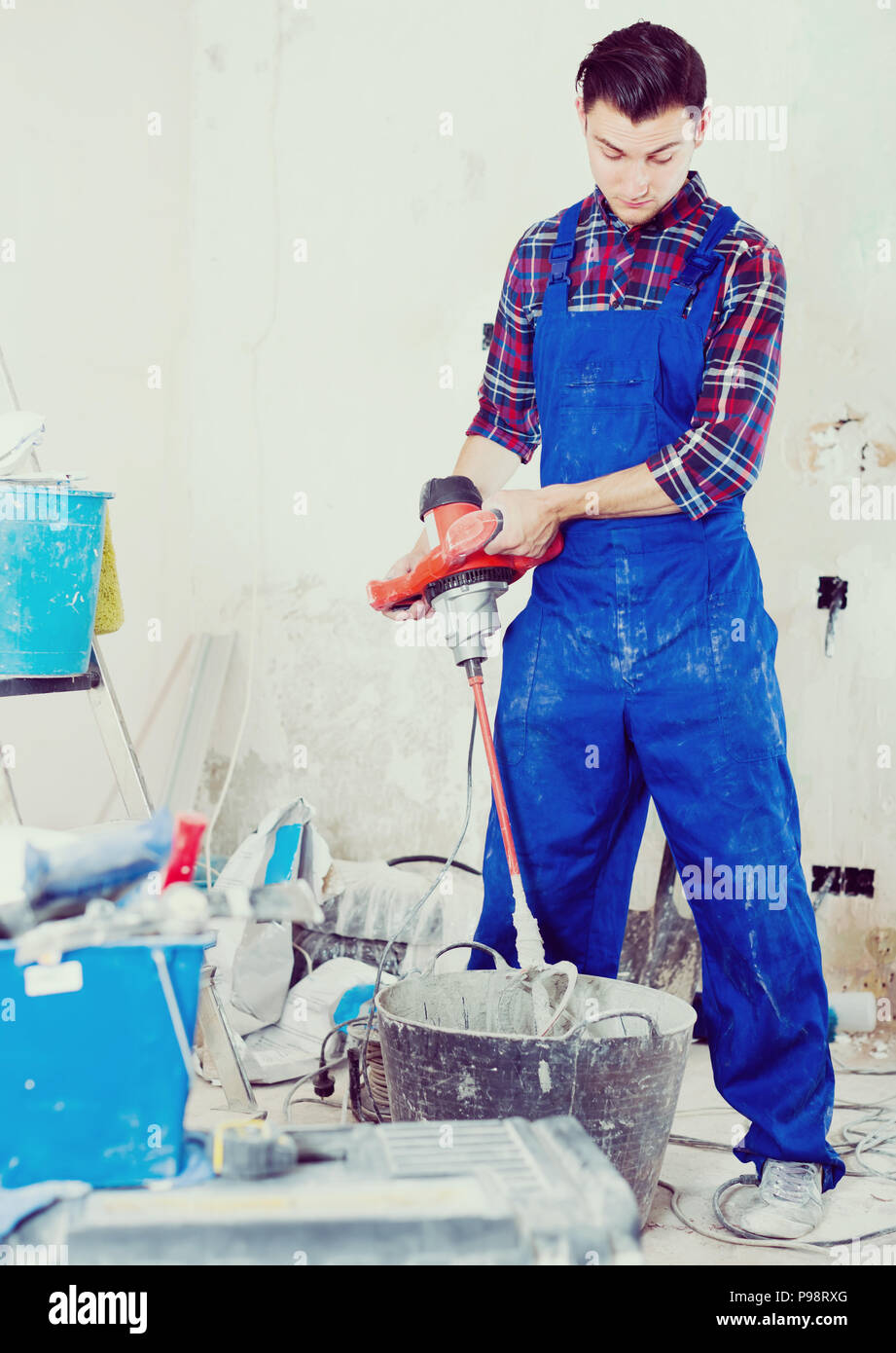 attentive builder mixing plaster in bucket using electric mixer in ...