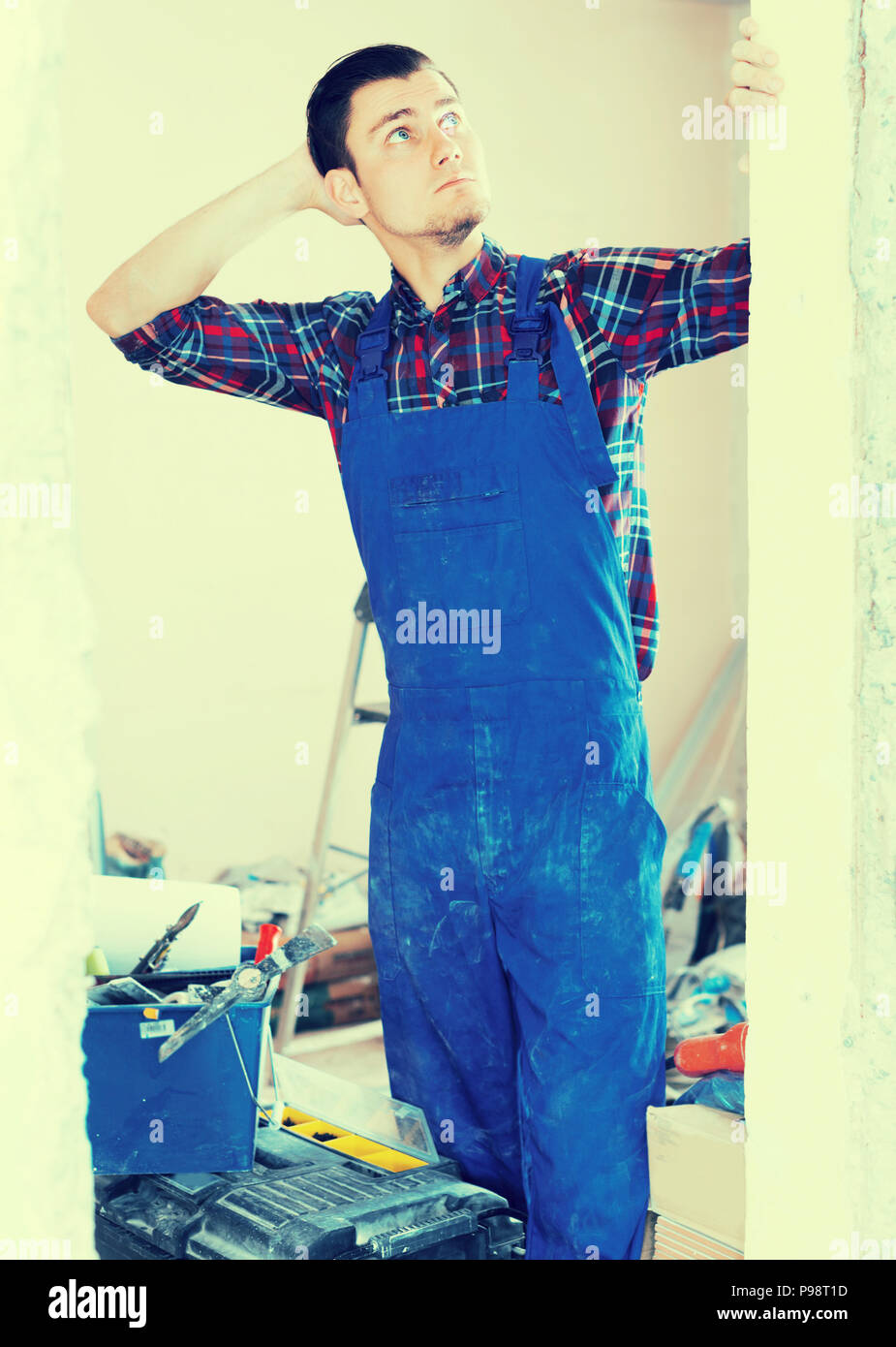 Puzzled young builder handyman examining room and planning renovation ...