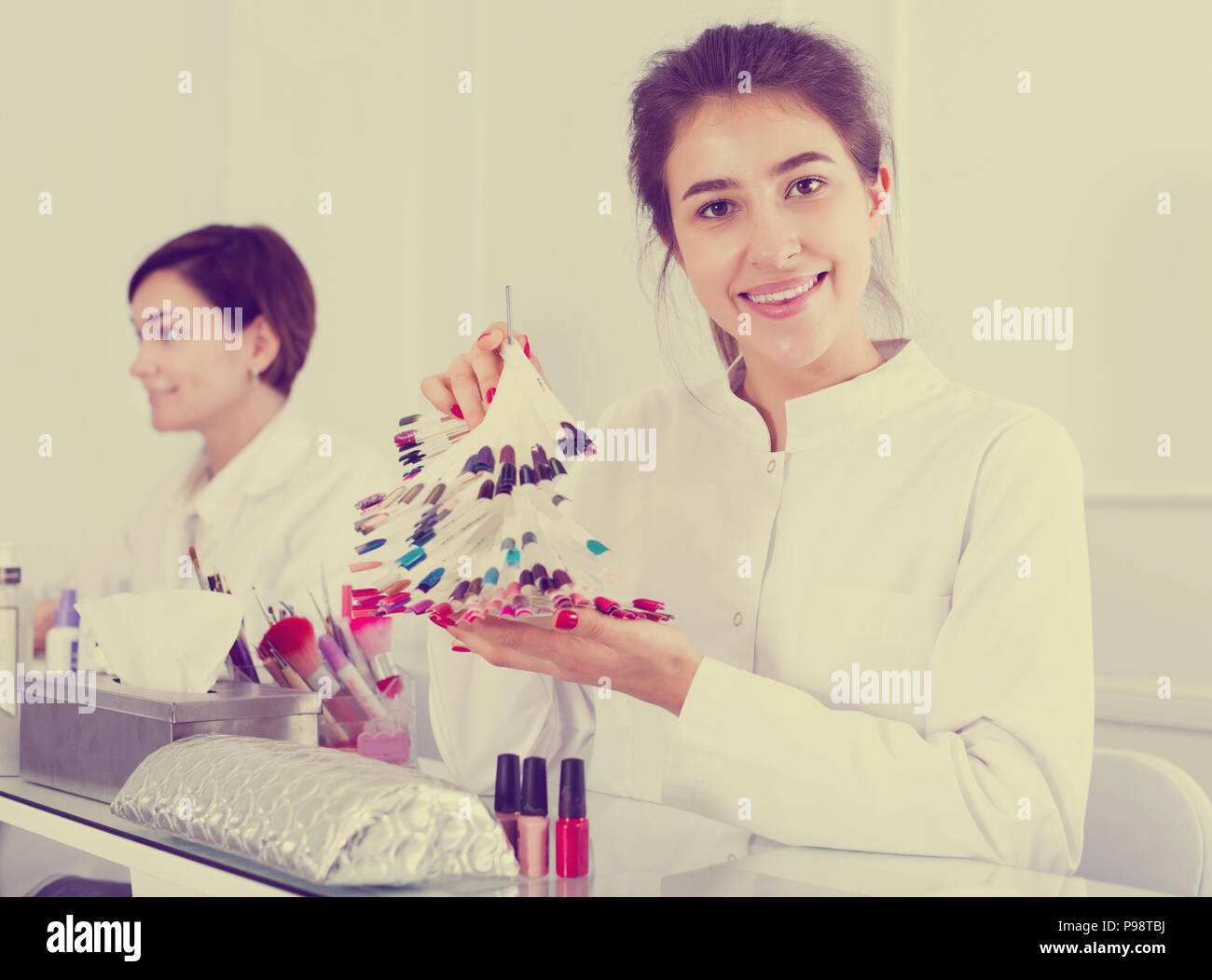 Pretty young girl doing nails displaying her workplace in nail salon ...