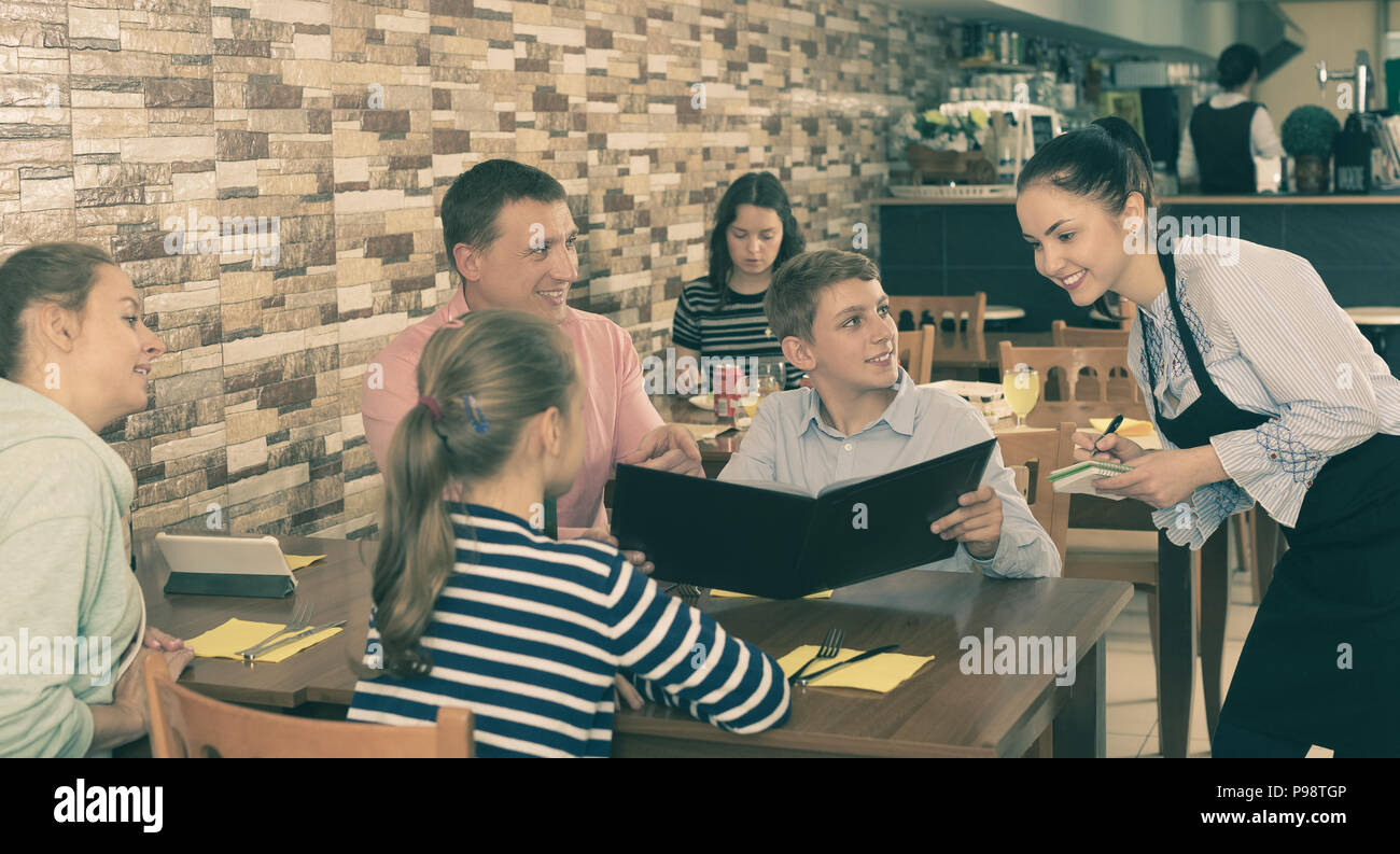 Positive cheerful waitress taking order from guests and writing into ...
