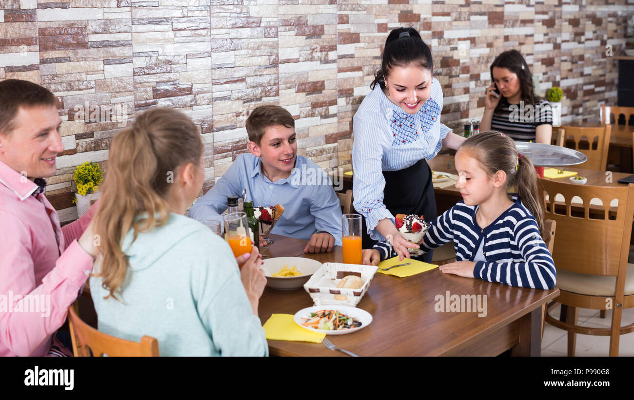 Girl is bringing delicious dessert to young visitors of family cafe ...