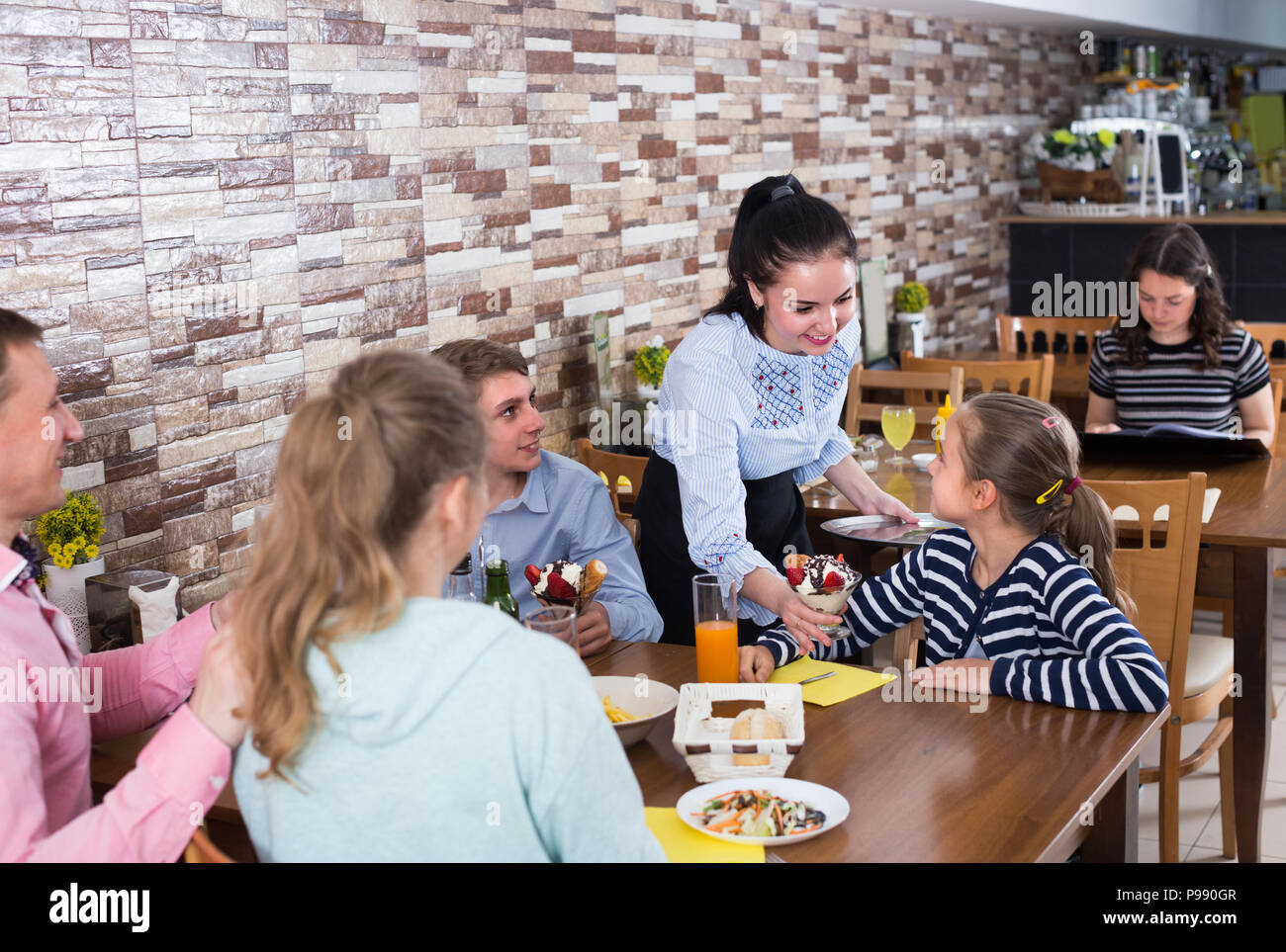 Smiling female is bringing delicious dessert to young visitors of ...