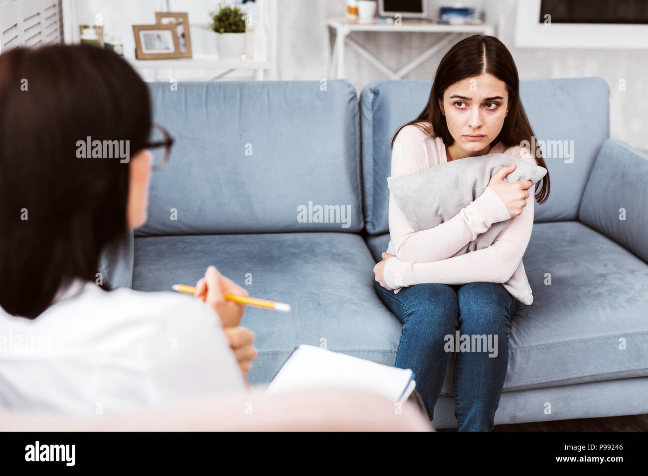 Young woman hugging a cushion and looking scared Stock Photo - Alamy